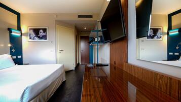 Quarto de hotel com uma cama, televisão fixada na parede e detalhes em painel de madeira.