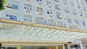 Hotel EMBAJADOR com fachada moderna, amplas janelas de vidro e entrada imponente.