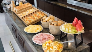 Buffet com diversos alimentos, incluindo pão, presunto, frutas e uma melancia.