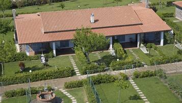 Um edifício grande com telhado de cerâmica, rodeado por jardins bem cuidados e um elemento decorativo circular de pedra.