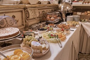 Buffet com diversos alimentos, incluindo queijo, frutas e pastelaria.