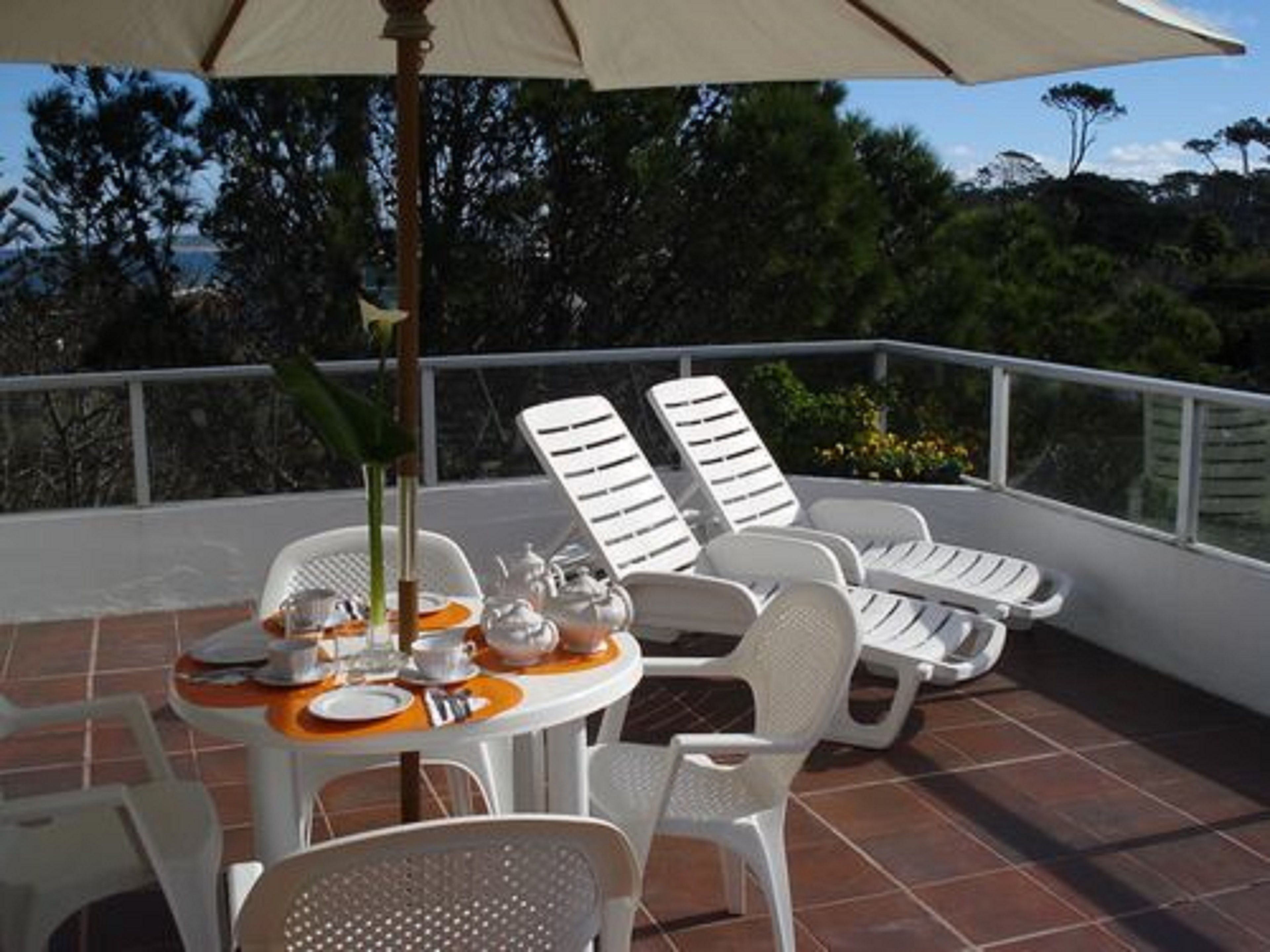 Terraço com mesa posta para dois, cadeiras brancas e guarda-sol.