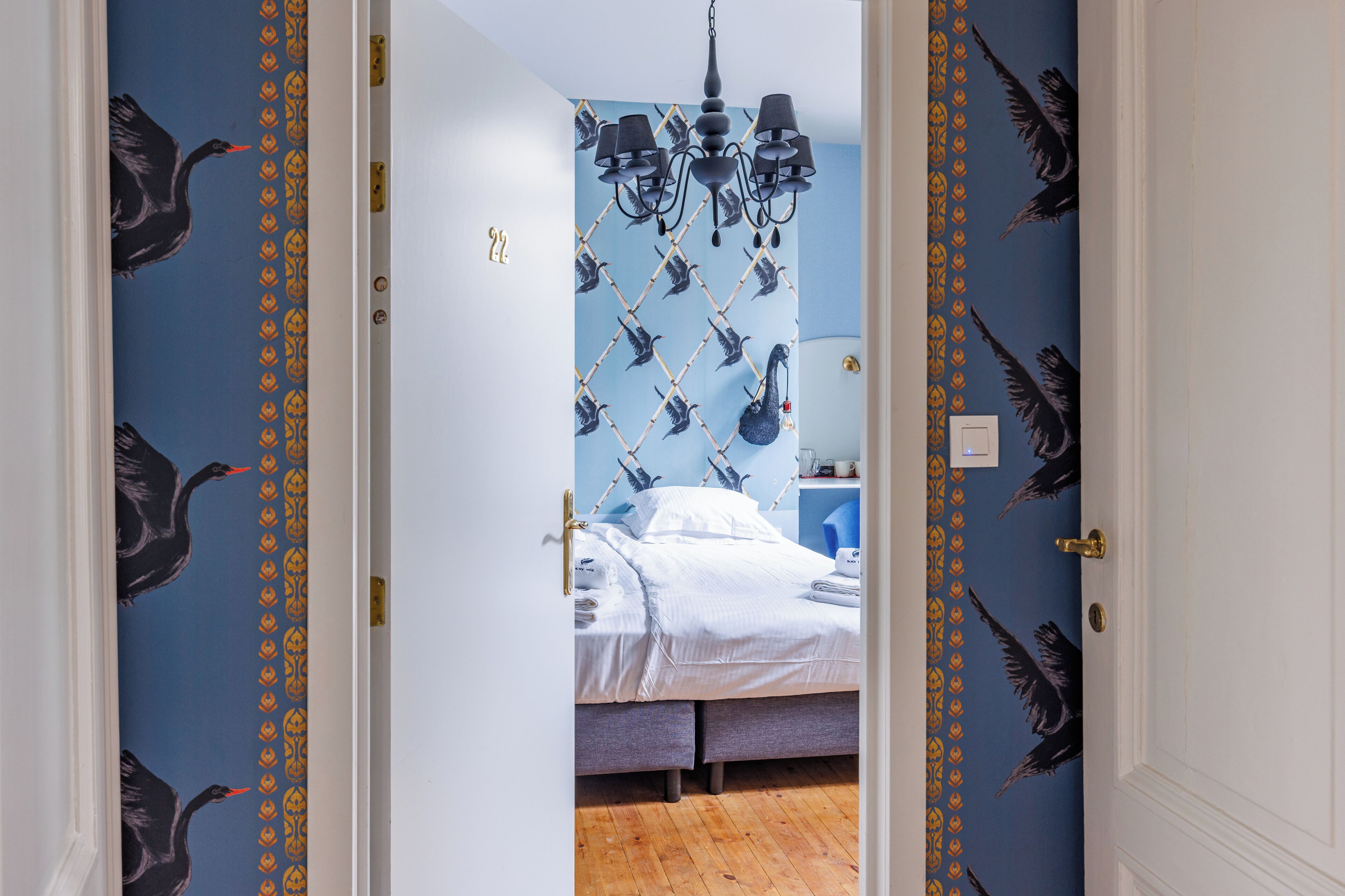 Um quarto com cama, lustre e parede com desenho de pássaros.