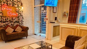 Um lobby com um sofá, uma mesa de centro de vidro, um candelabro, uma televisão e um letreiro de neon com a inscrição 'Paris Opéra'.