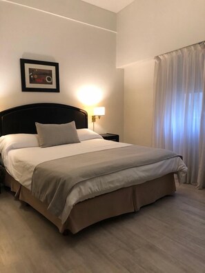 Uma cama bem arrumada com cabeceira, abajur e quadro na parede.