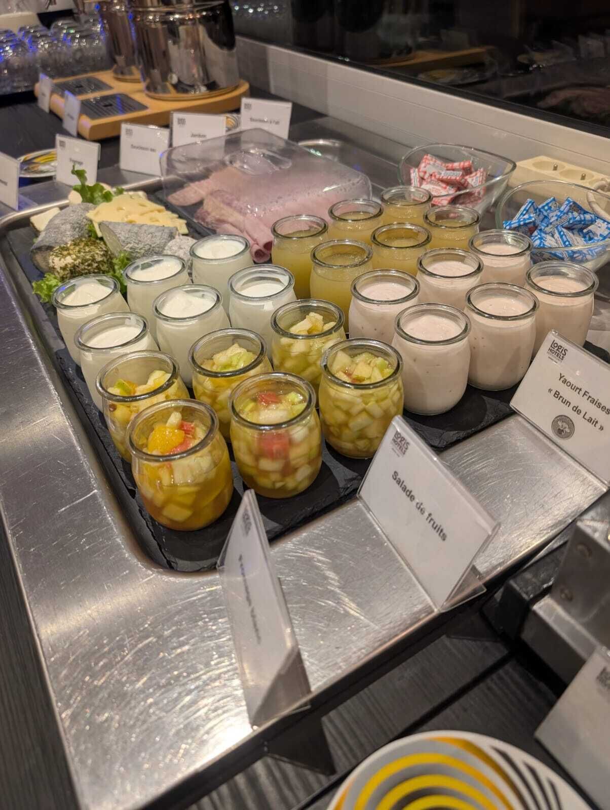 Buffet com diversos alimentos, incluindo potes de salada de frutas, iogurte e queijo.