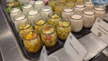 Buffet com diversos alimentos, incluindo potes de salada de frutas, iogurte e queijo.