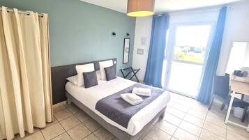 Quarto de hotel com cama, escrivaninha, cadeira, espelho e vista exterior.