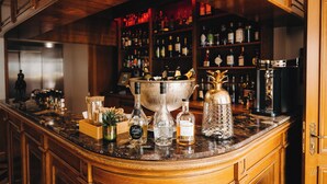 Uma área de bar com armários de madeira, bancada de mármore e diversos frascos e copos.