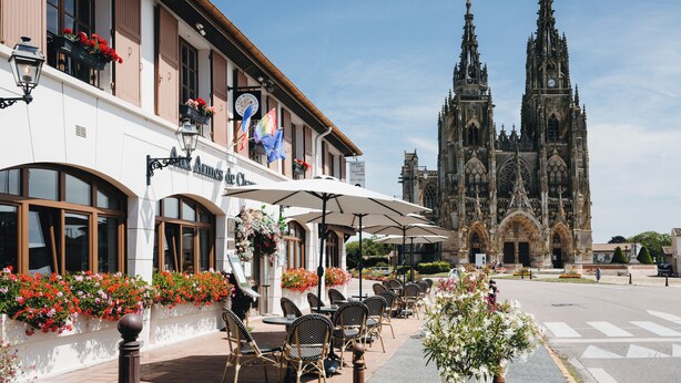 Um restaurante com mesas ao ar livre e uma catedral ao fundo.