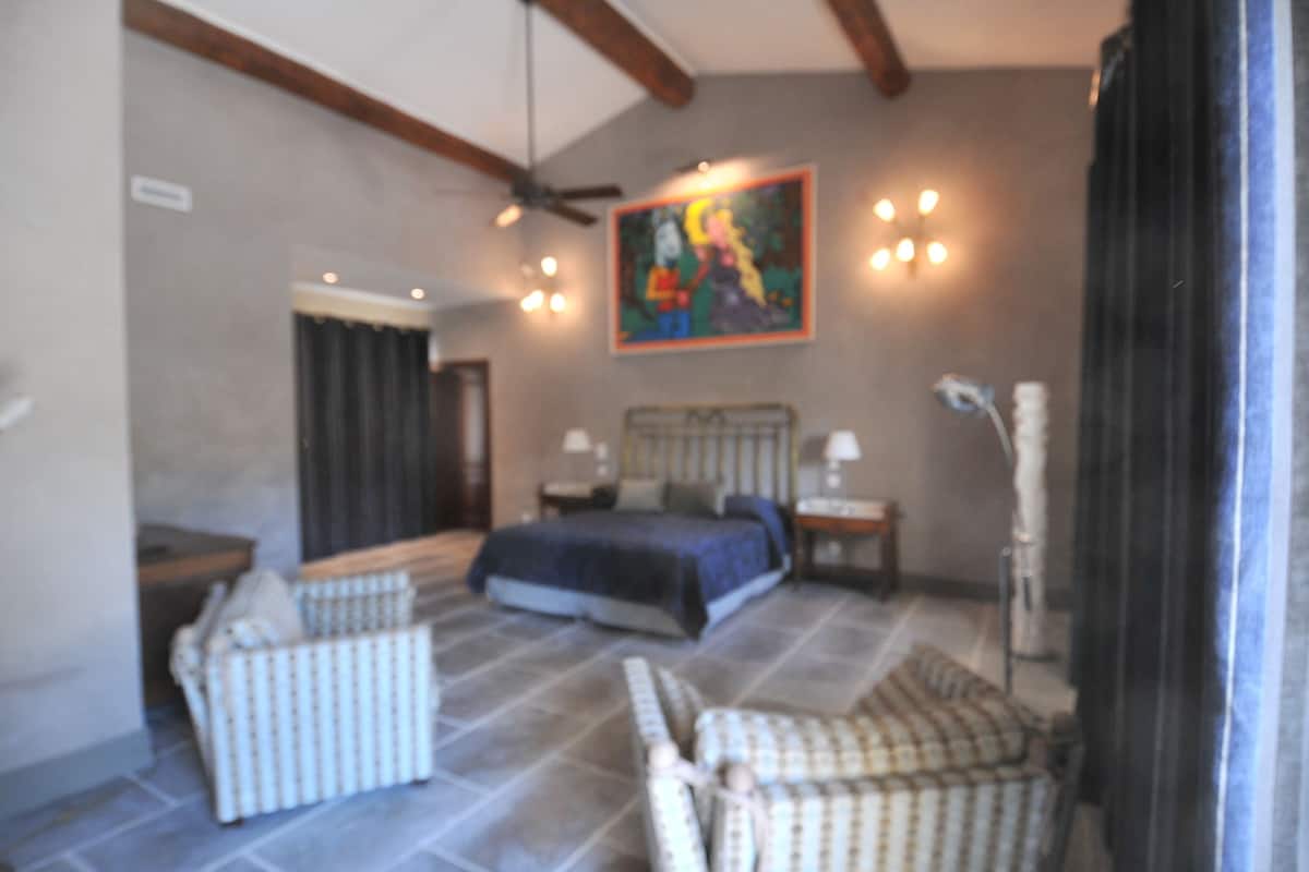 Quarto com cama, duas mesas de cabeceira, ventilador de teto e um quadro na parede.