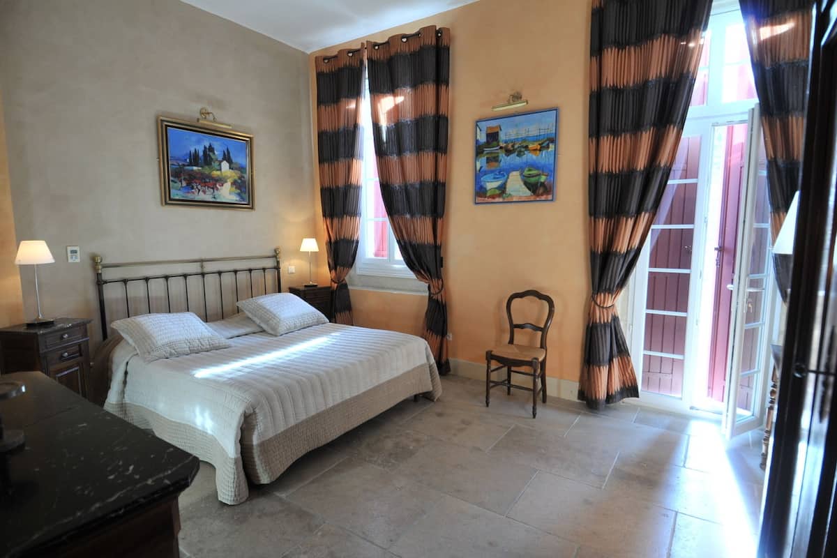 Quarto com cama, duas mesas de cabeceira, uma cadeira e janela com cortinas.