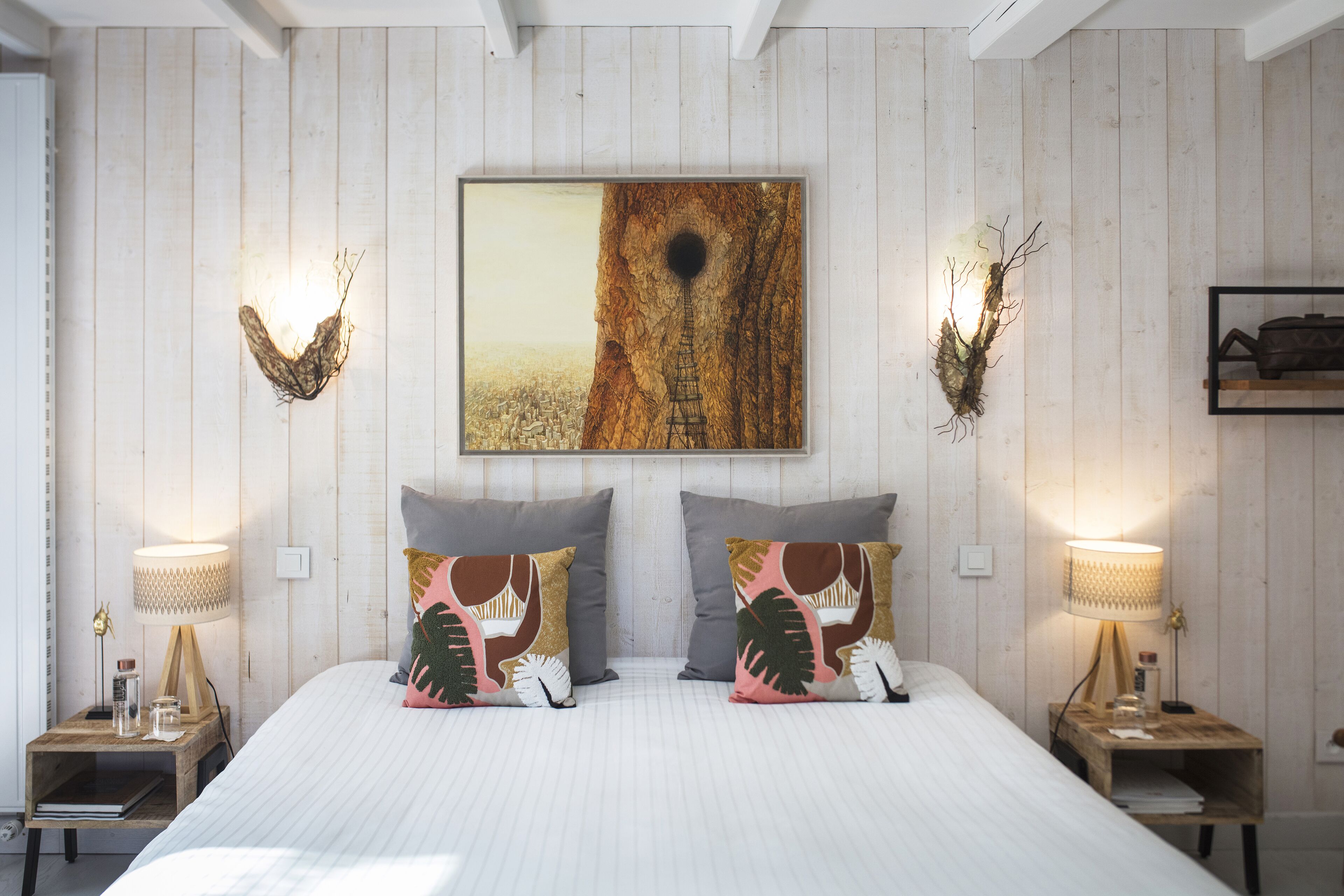 Quarto com cama grande, duas mesinhas de cabeceira, obra de arte na parede e cabeceira de madeira.