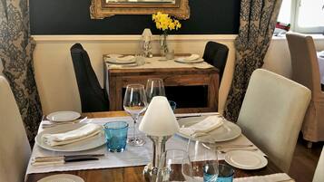Uma sala de jantar com uma mesa posta para seis pessoas, incluindo pratos, copos e talheres. Um espelho está pendurado acima da mesa, e há um vaso com flores amarelas sobre ela.