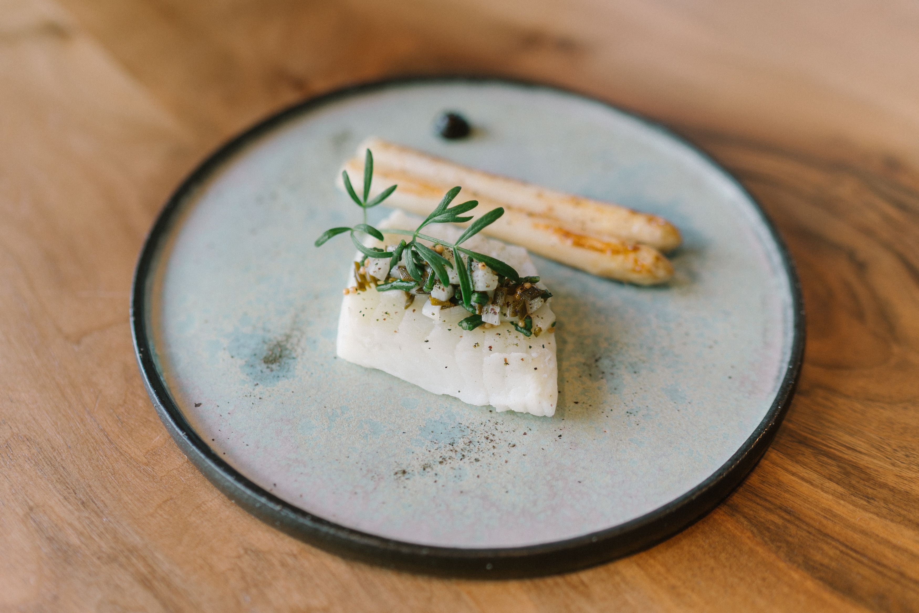 Um prato com um alimento branco decorado com ervas, sobre um prato de cerâmica redondo.