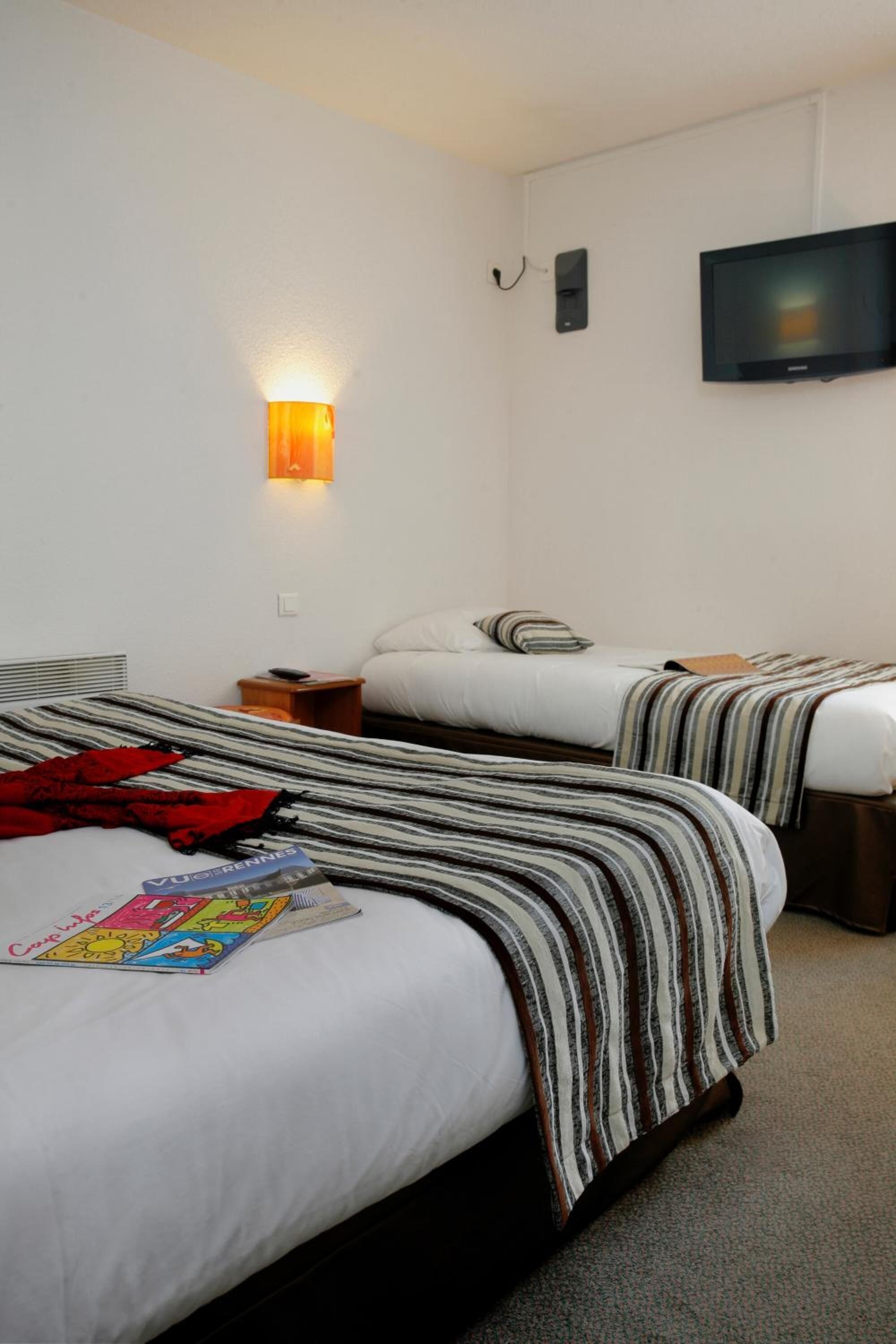 Quarto de hotel com duas camas, TV de tela plana e luminária fixada na parede.