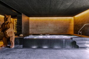 Uma área de spa com hidromassagem, parede de pedra e uma escultura.