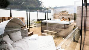 Um quarto ao ar livre moderno com uma banheira de hidromassagem com paredes de vidro, um sofá de vime e uma cama com dossel.