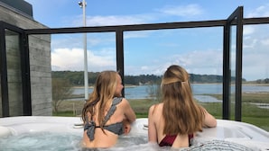 Duas mulheres em uma banheira de hidromassagem com vista para um lago e árvores.