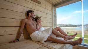 Duas pessoas sentadas em bancos de madeira num quarto com uma grande janela com vista para uma praia.