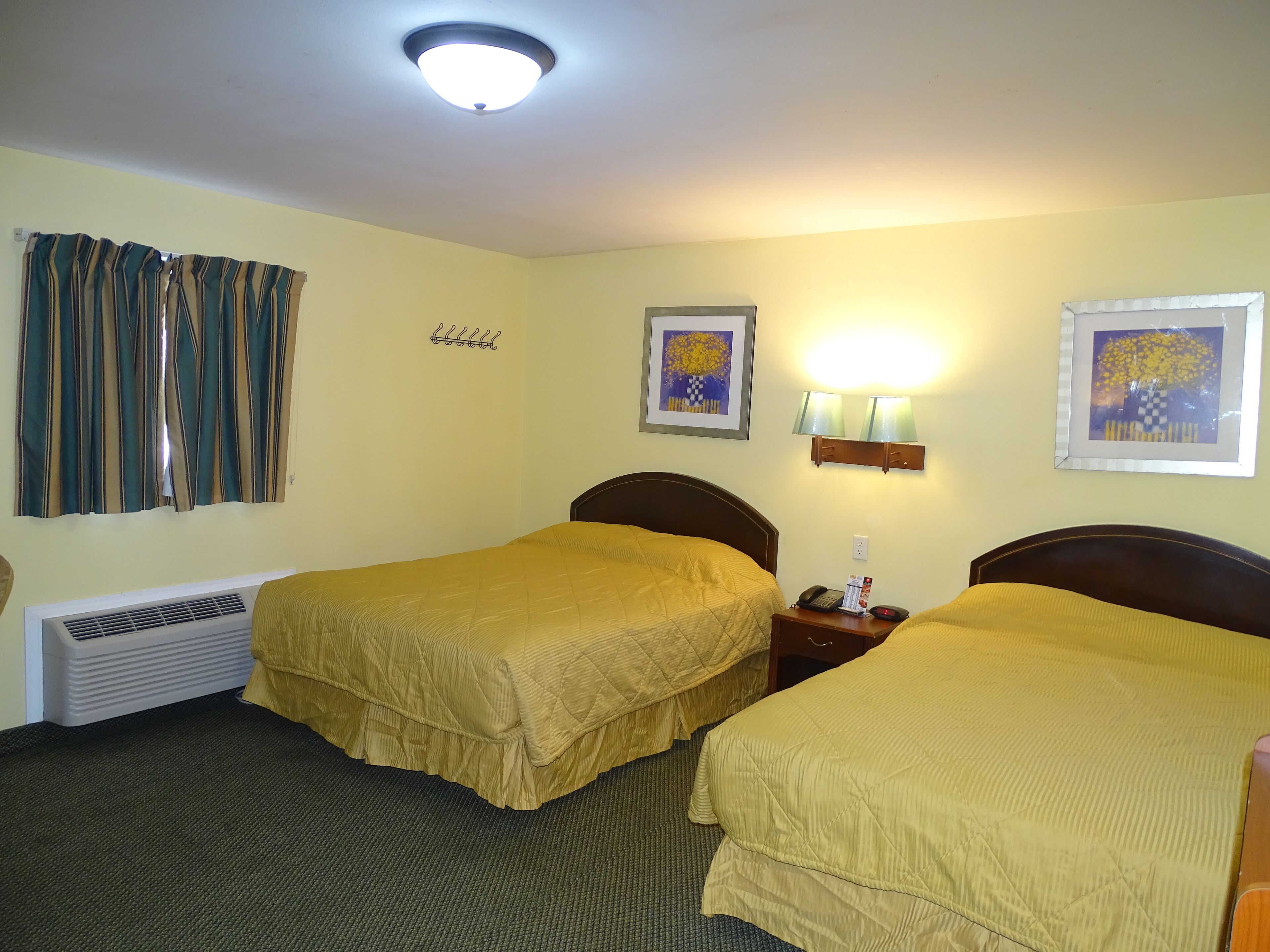 Quarto de hotel com duas camas, aquecedor, luminária e obras de arte nas paredes.