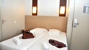 Quarto de hotel com duas camas, cabeceira de madeira e duas luzes fixadas na parede.