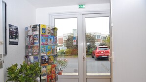 Uma área de recepção com porta de vidro, uma planta e uma pilha de revistas.