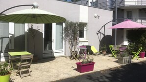 Uma área externa com mesas, cadeiras, guarda-sóis e plantas em vasos.