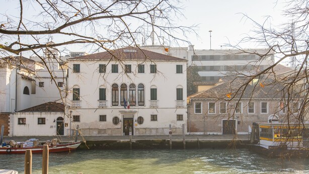 Um edifício à beira-mar com estilo arquitetônico tradicional, um canal com barcos e uma vista clara da água.