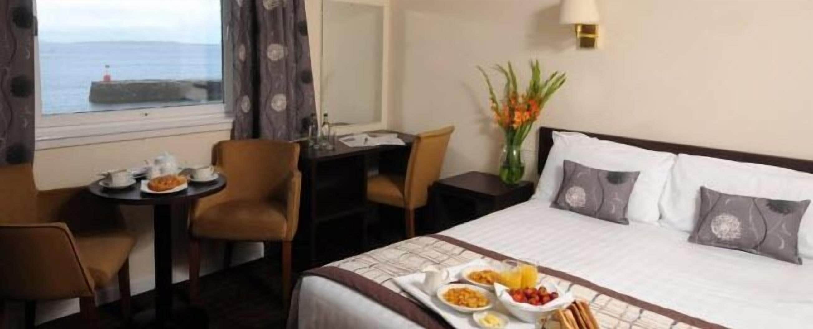 Quarto de hotel com uma cama, mesa de jantar com cadeiras, pequena escrivaninha e vista para o mar.