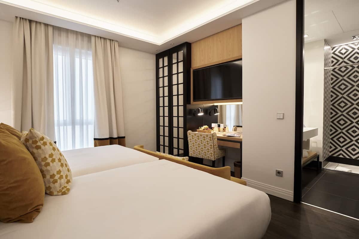 Quarto de hotel com uma cama grande, uma escrivaninha com cadeira, televisão e banheiro visível através de uma porta aberta.