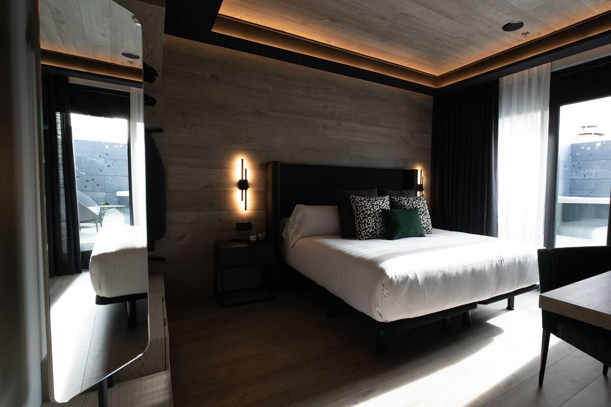 Quarto de hotel moderno com cama grande, mesas de cabeceira, escrivaninha e vista para a cidade.