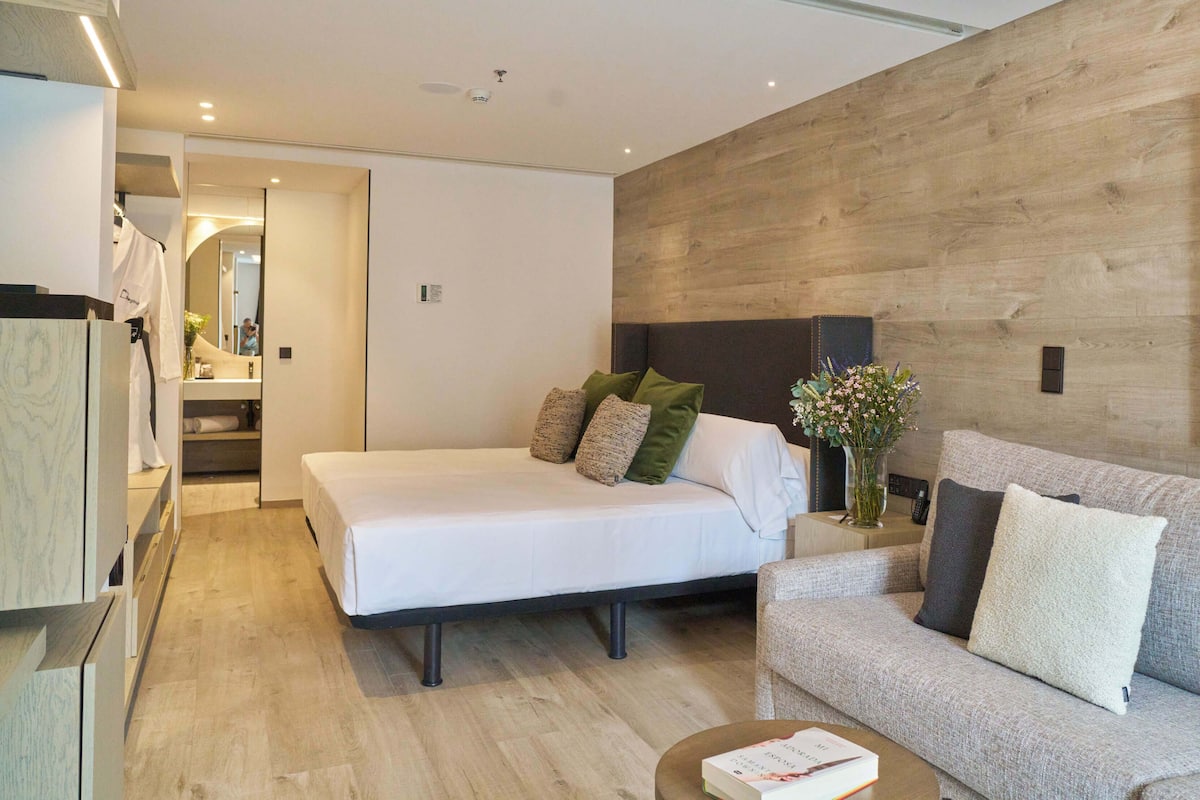 Quarto de hotel moderno com cama, sofá, mesinha e espelho.