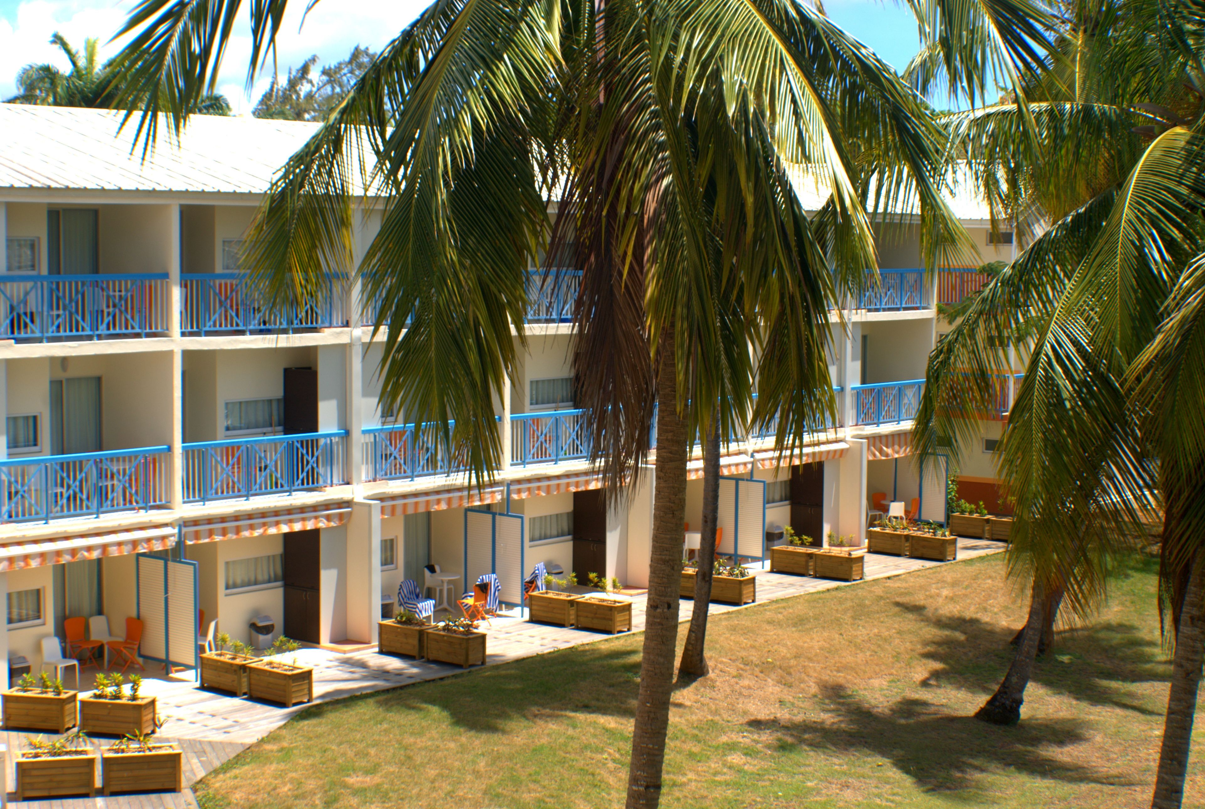 Um hotel de vários andares com varandas, área de estar externa e palmeiras.