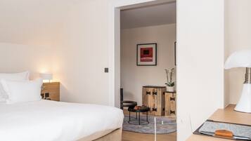 Quarto de hotel com cama, mesa de cabeceira, abajur e escrivaninha com luminária.