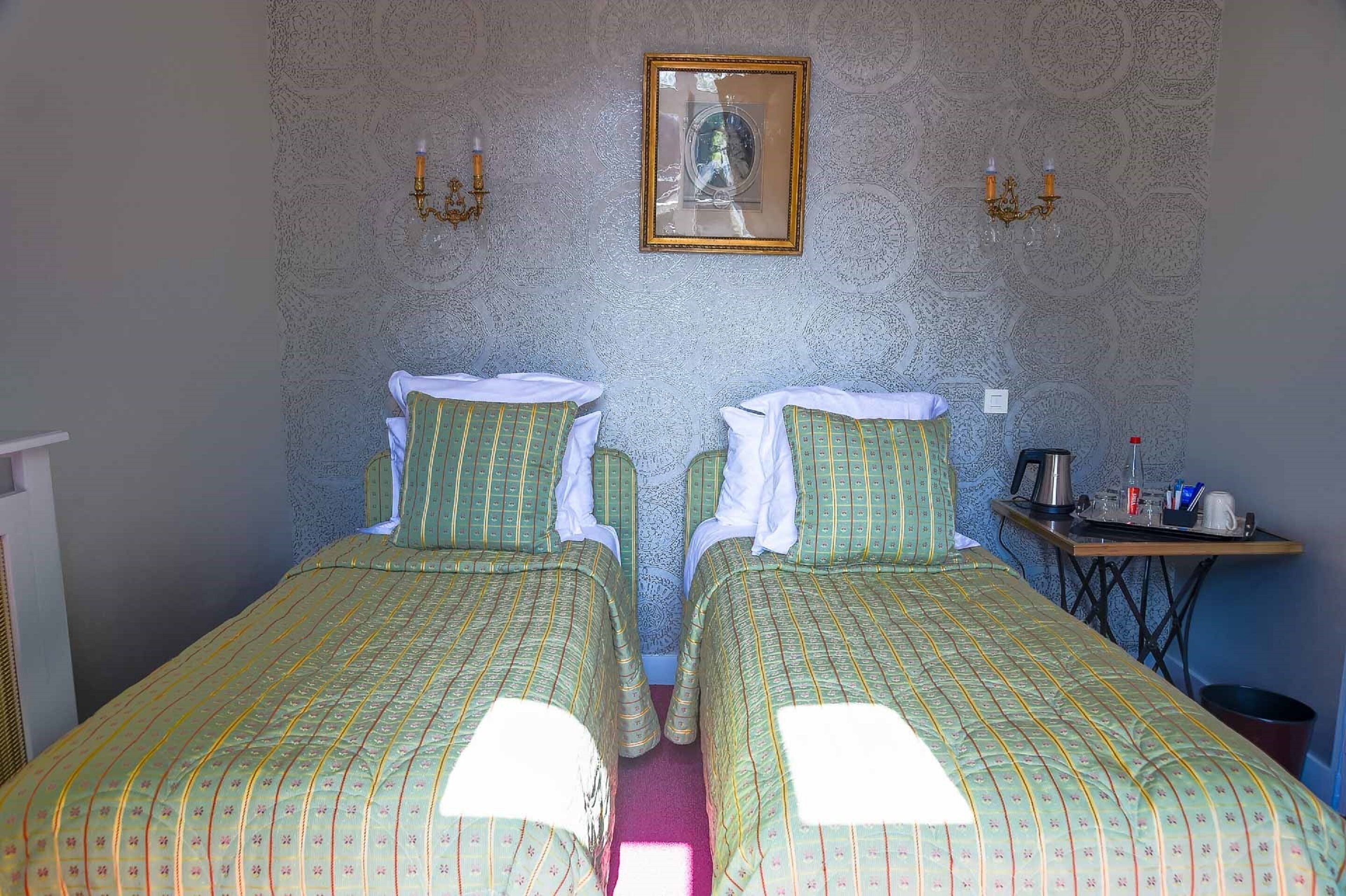 Quarto com duas camas, uma mesa com chaleira e um relógio de parede.