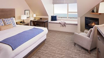 Quarto de hotel com cama grande, escrivaninha, cadeira, sofá, lareira e janela com vista para o mar.