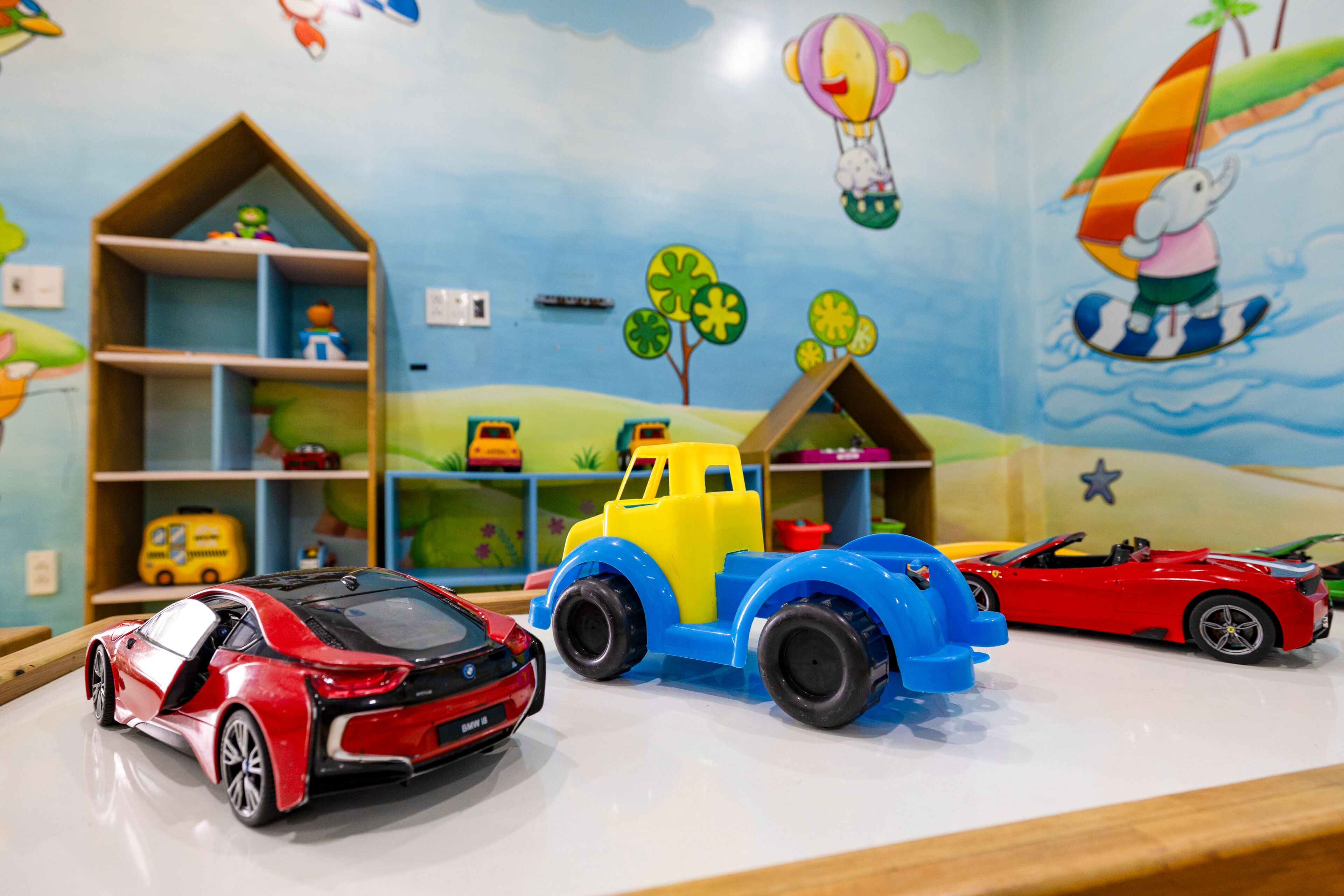 Quarto com uma mesa branca exibindo carrinhos de brinquedo e um mural colorido na parede.