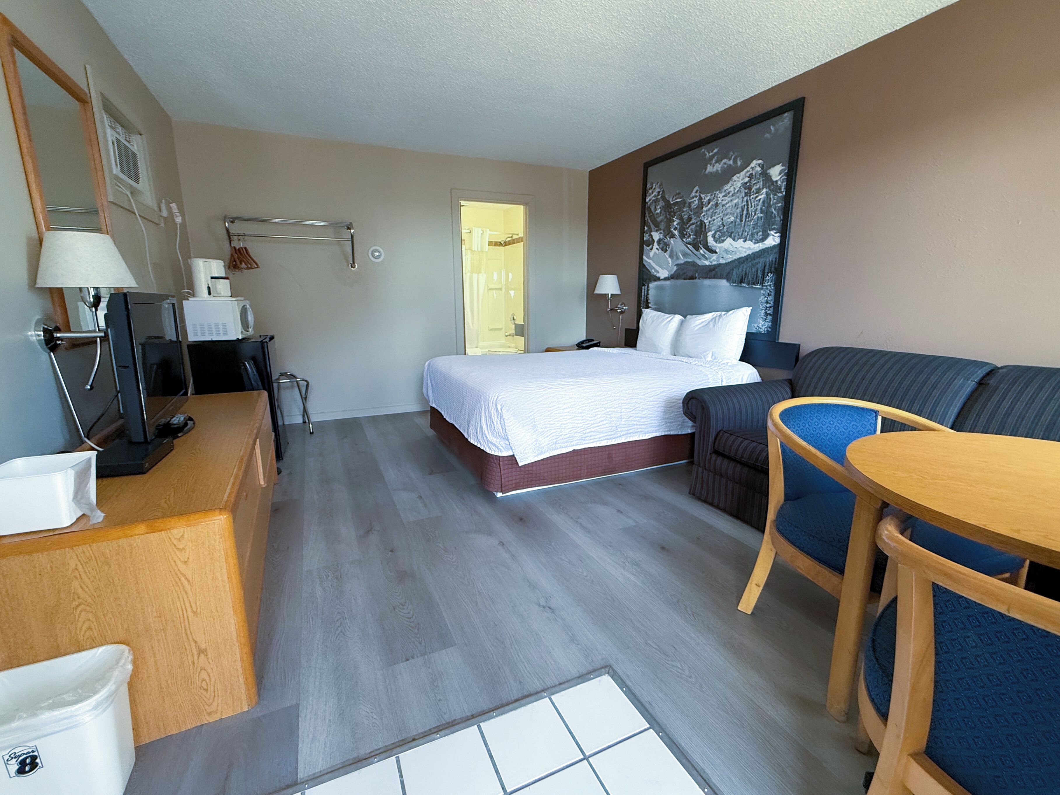 Quarto de hotel com uma cama, uma escrivaninha com computador, uma cadeira, um sofá e um quadro na parede.