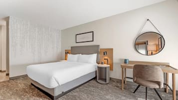 Quarto de hotel moderno com cama, escrivaninha, cadeira e espelho fixado na parede.