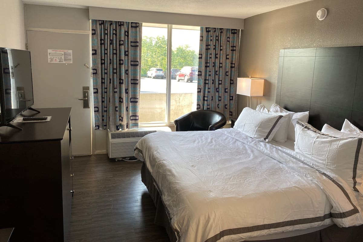 Quarto de hotel com cama, escrivaninha com televisão, uma cadeira e janela com cortinas.