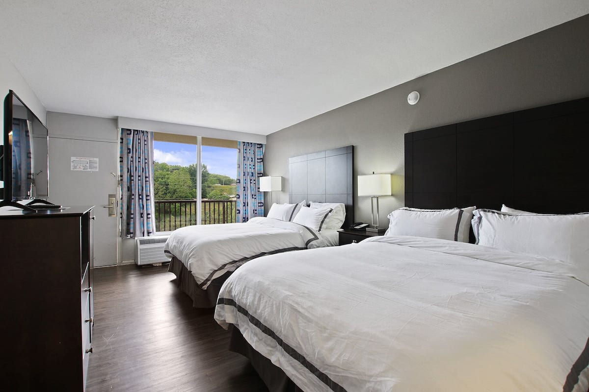 Quarto de hotel com duas camas, uma mesa de trabalho e vista para o exterior.