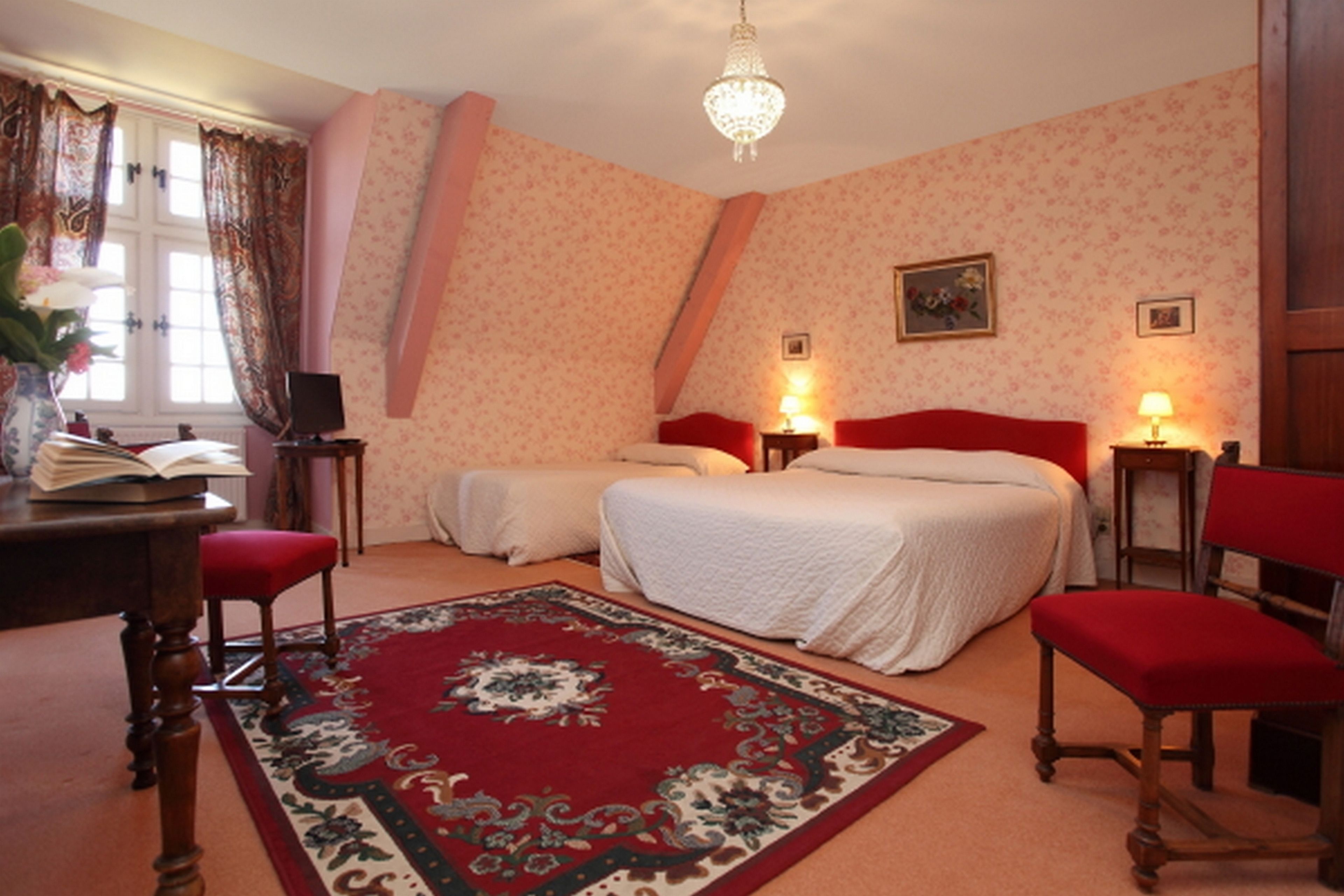 Quarto com duas camas, um candelabro e um tapete com padrão vermelho e branco.