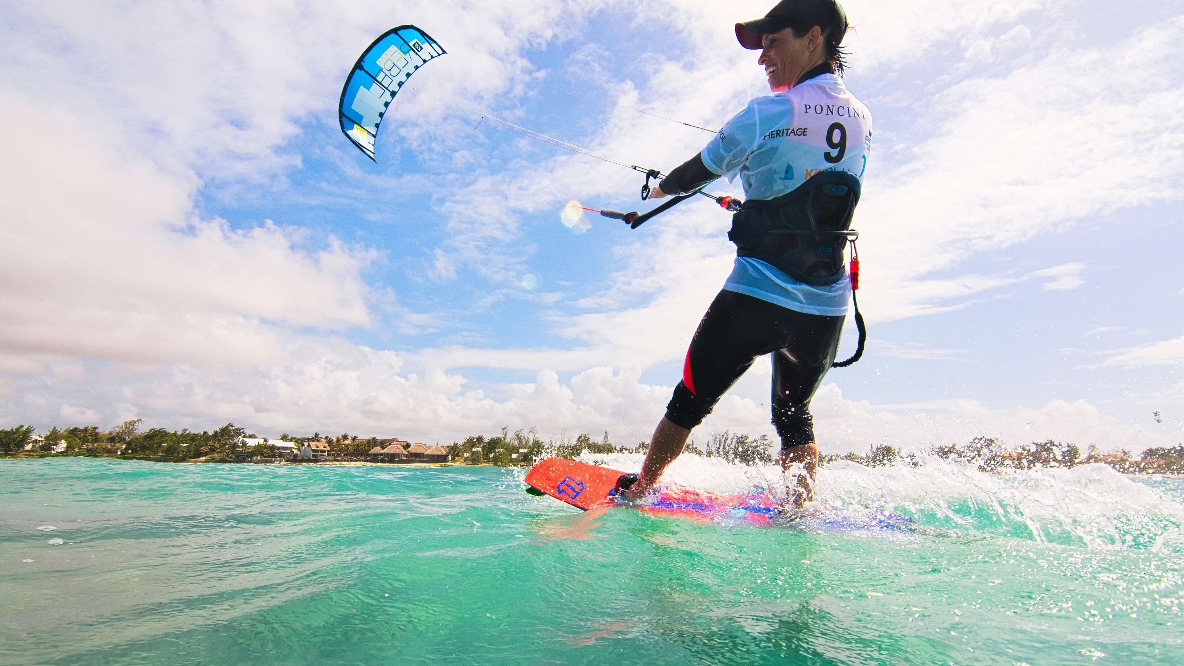 Uma pessoa praticando kitesurf em águas turquesa sob um céu claro.