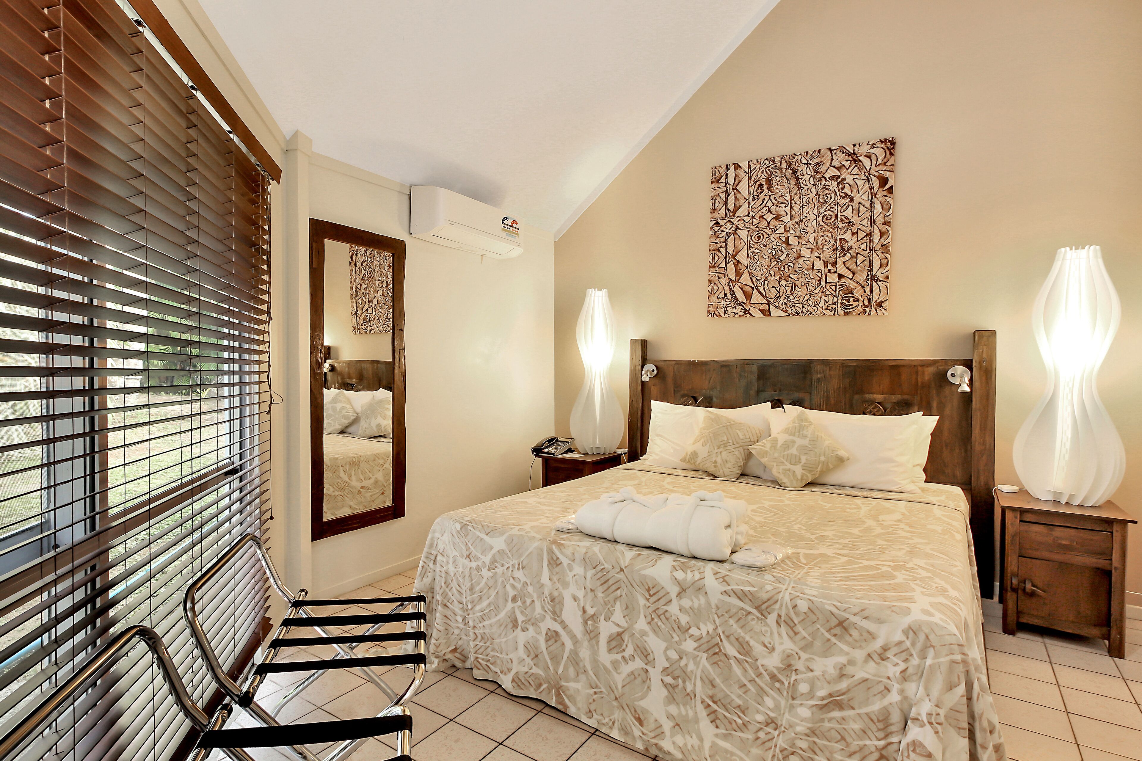 Quarto com uma cama grande, cabeceira de madeira, mesa de cabeceira com abajur e ar condicionado fixado na parede.