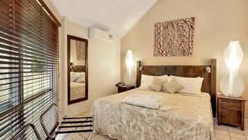 Quarto com uma cama grande, cabeceira de madeira, mesa de cabeceira com abajur e ar condicionado fixado na parede.