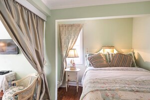 Quarto com cama, mesa de cabeceira, luminária e cortinas.