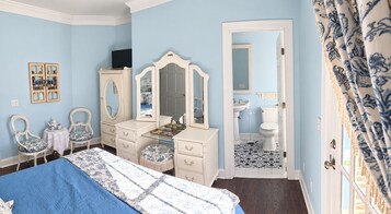 Quarto com cama, penteadeira, cadeiras e banheiro visível por uma porta aberta.