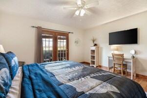 Quarto com uma cama grande, uma escrivaninha com cadeira, televisão e ventoinha no teto.