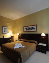 Quarto de hotel com uma cama, duas mesas de cabeceira, uma escrivaninha, uma cadeira e duas luminárias.